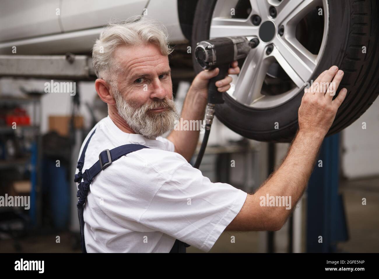 Senior bearded car mechanic smiling to the camera while working with ...
