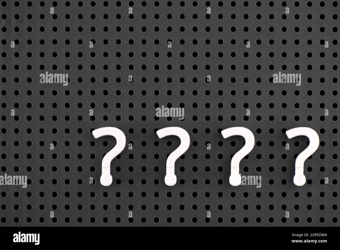 Four question marks spelled out by a white symbols on a gray pegboard ...