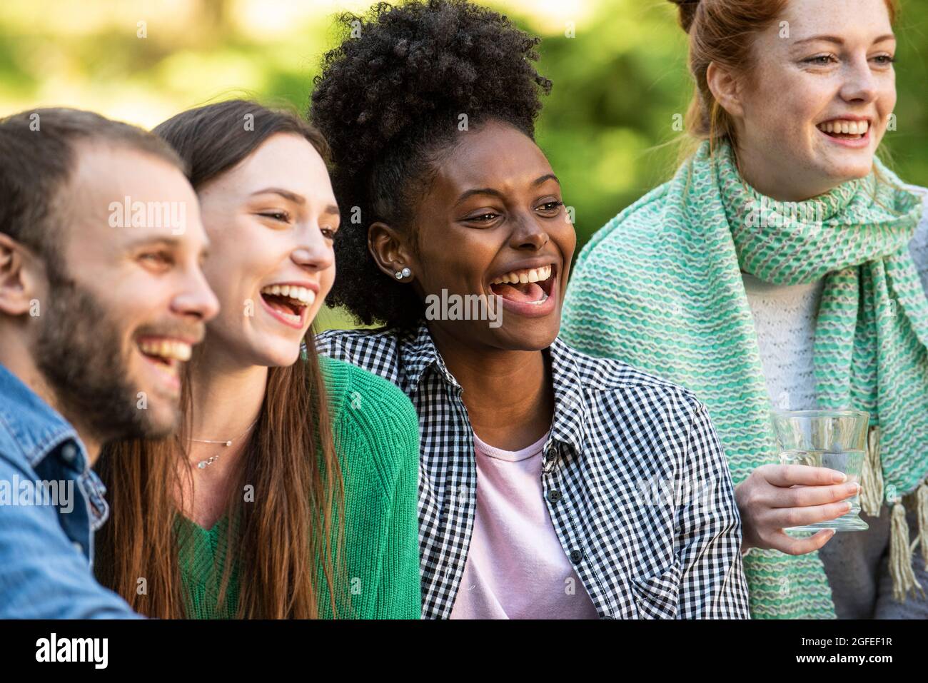 Smiling young friends sitting together in public park Stock Photo - Alamy