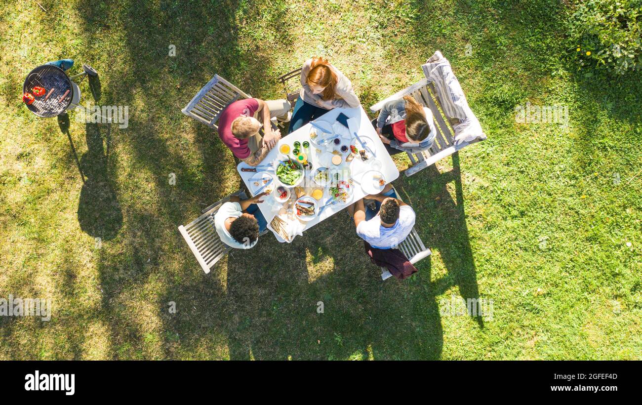 Happy young friends eating around a table in garden Stock Photo - Alamy