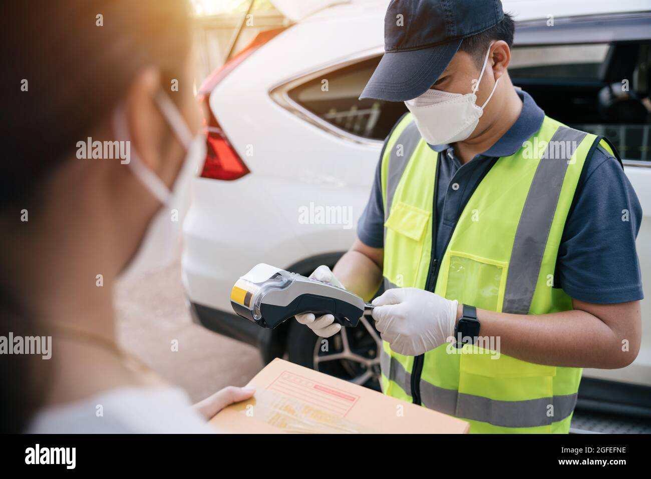 Asian delivery man using a credit card reader while delivering products ...