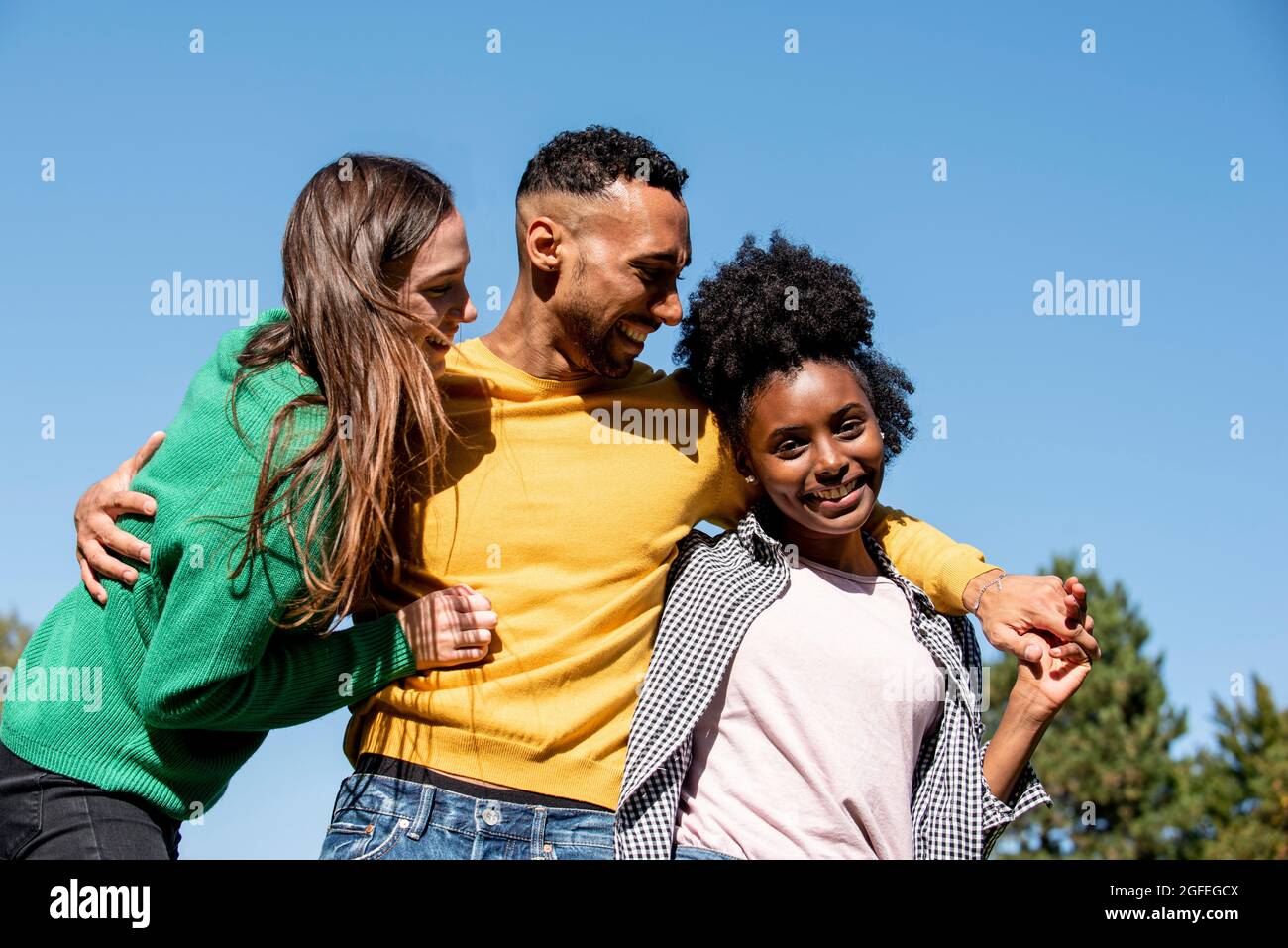 Portrait of smiling young friends standing with arm around in public ...