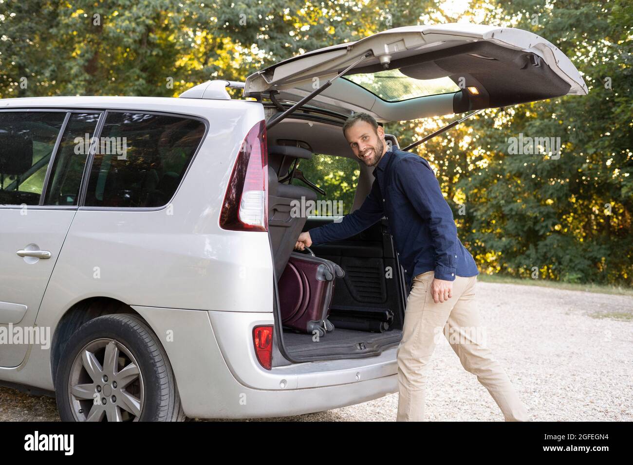 Young man loading bag in car trunk before a trip Stock Photo - Alamy