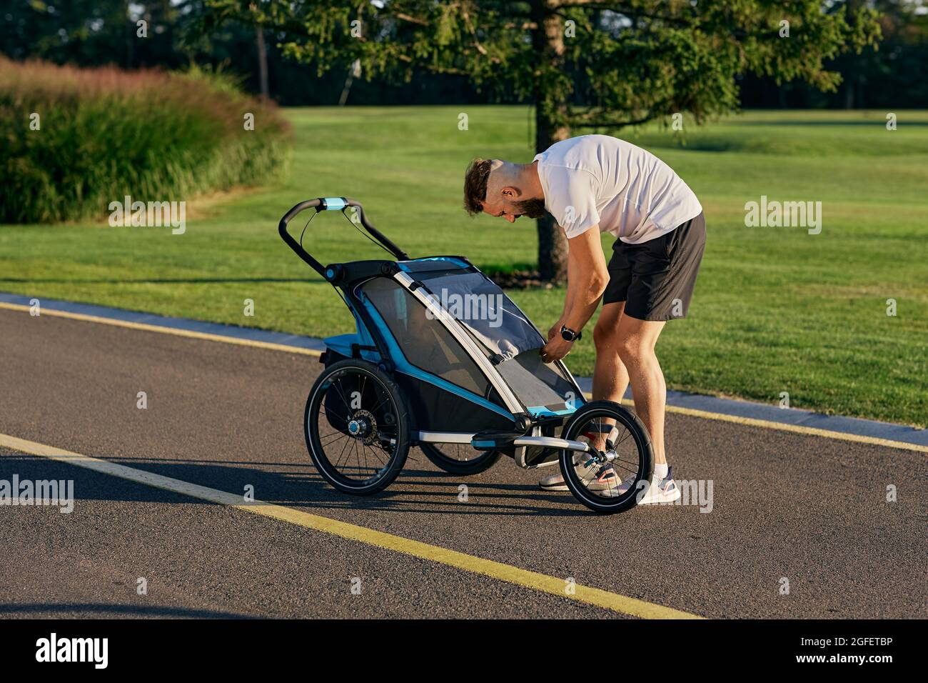 Young father is walking with his son in a baby carriage at city park ...