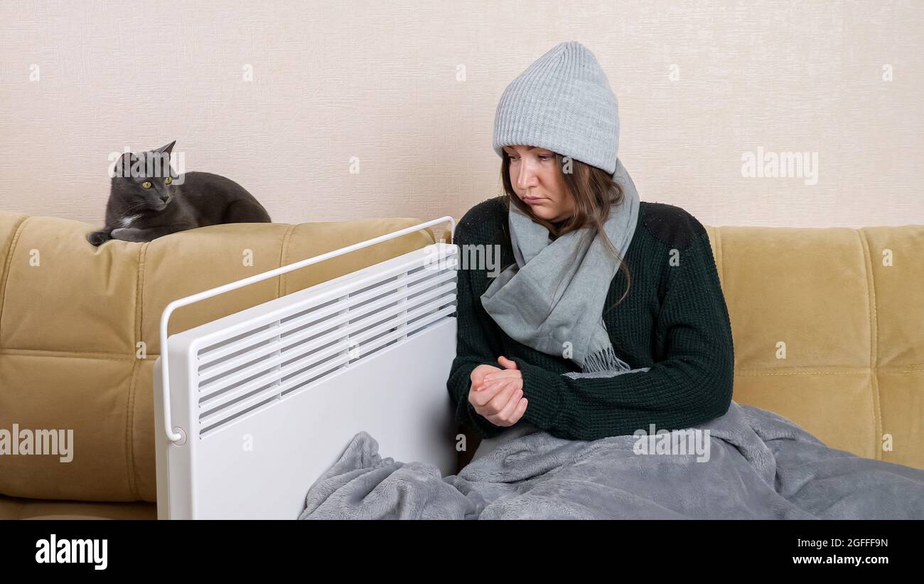 Frozen lady leans on heater sitting near cat on soft sofa Stock Photo ...
