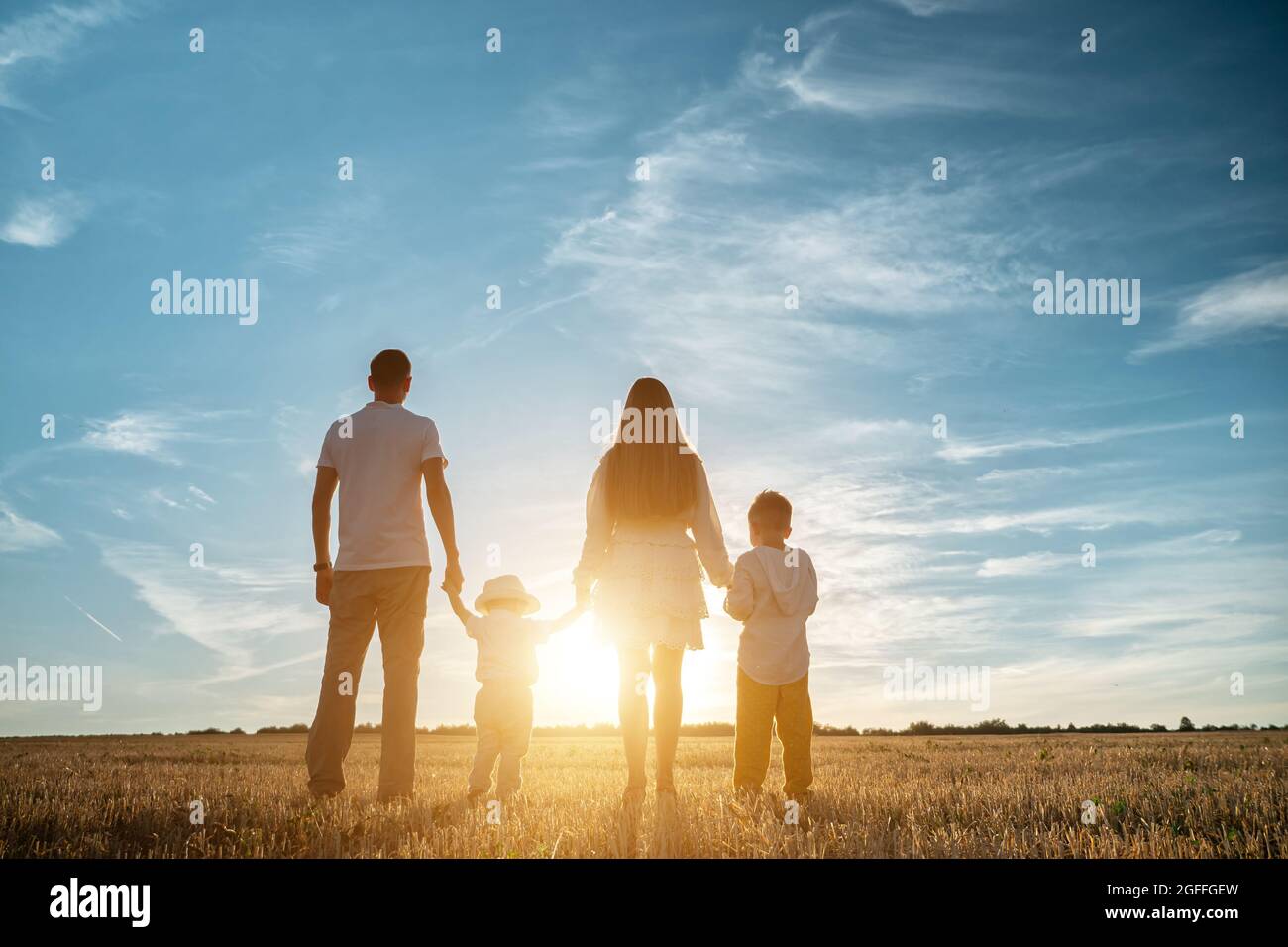 Family with children walks along fields at back setting sun Stock Photo ...
