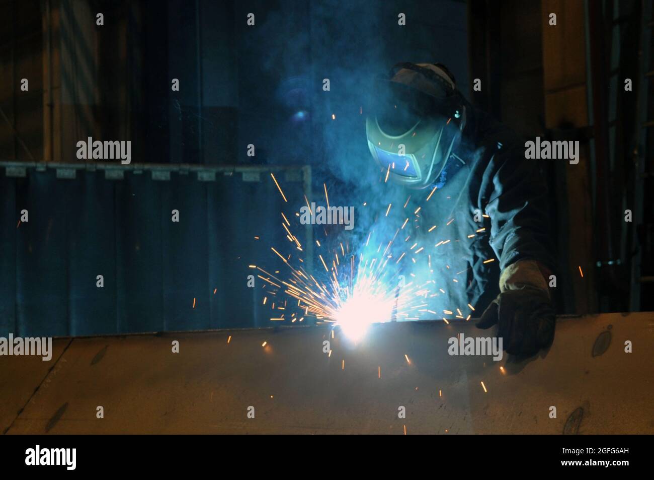 An electric welder welds metal structures at a factory. Professions ...