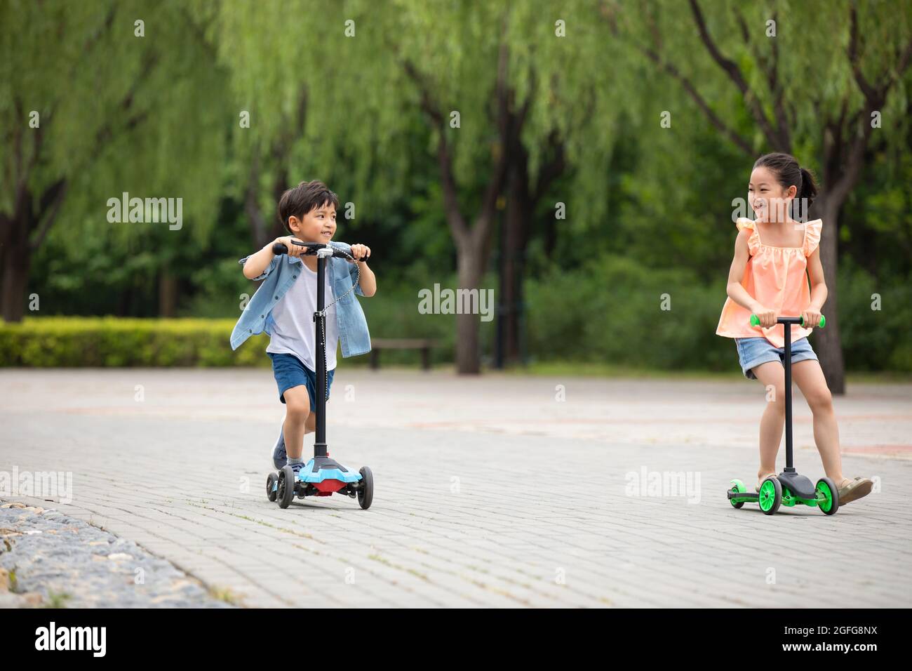 Happy children riding scooter in park Stock Photo - Alamy