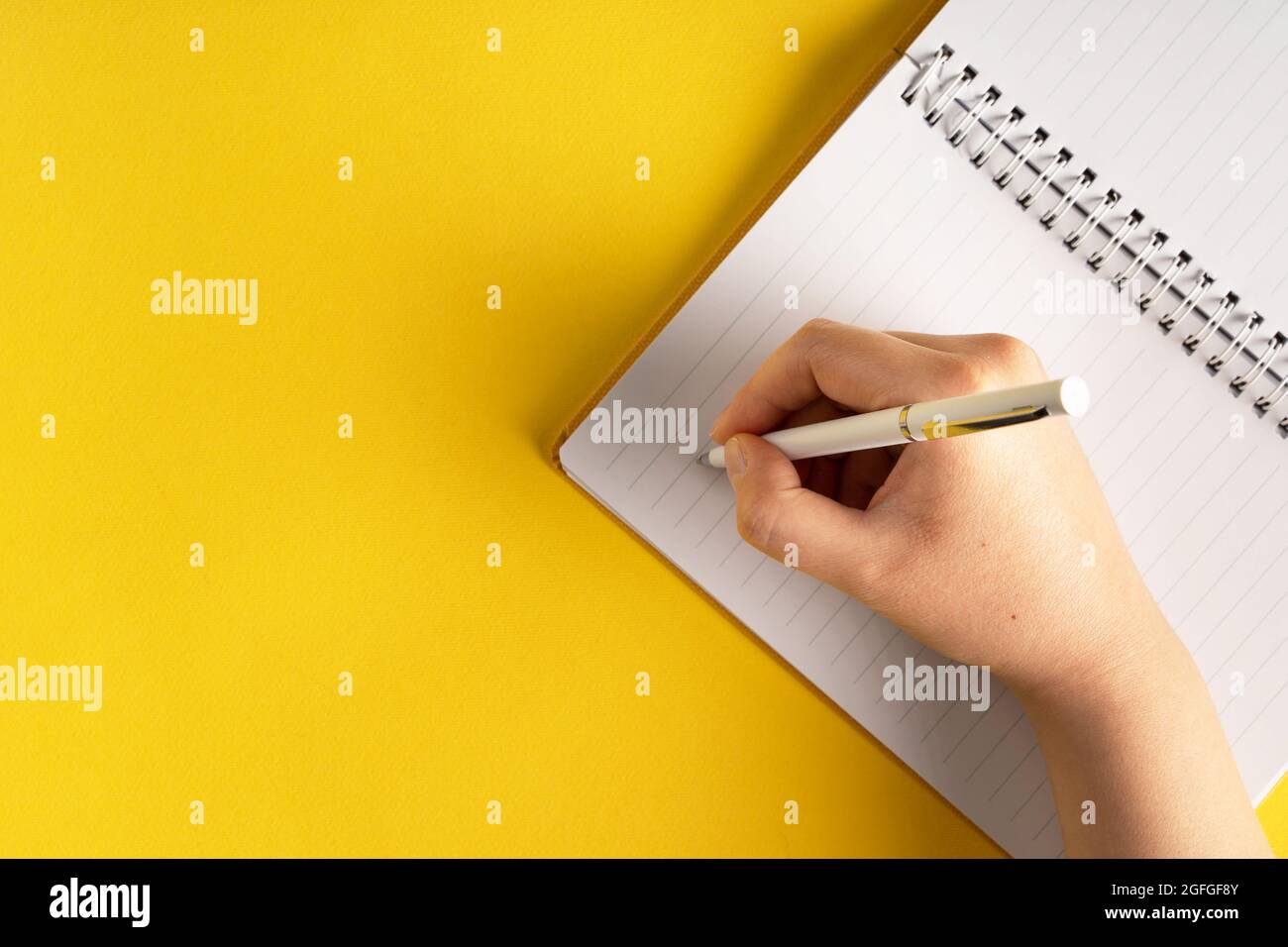 close up on hand holding pencil writing on notebook on yellow ...
