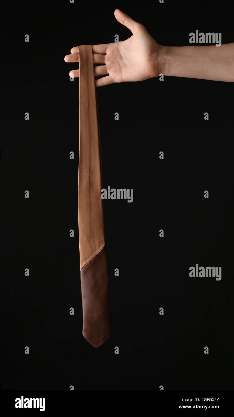 Female hand holding brown tie on black background Stock Photo - Alamy