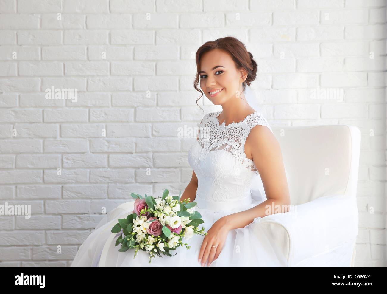 Beautiful bride with wedding bouquet on white brick wall background ...