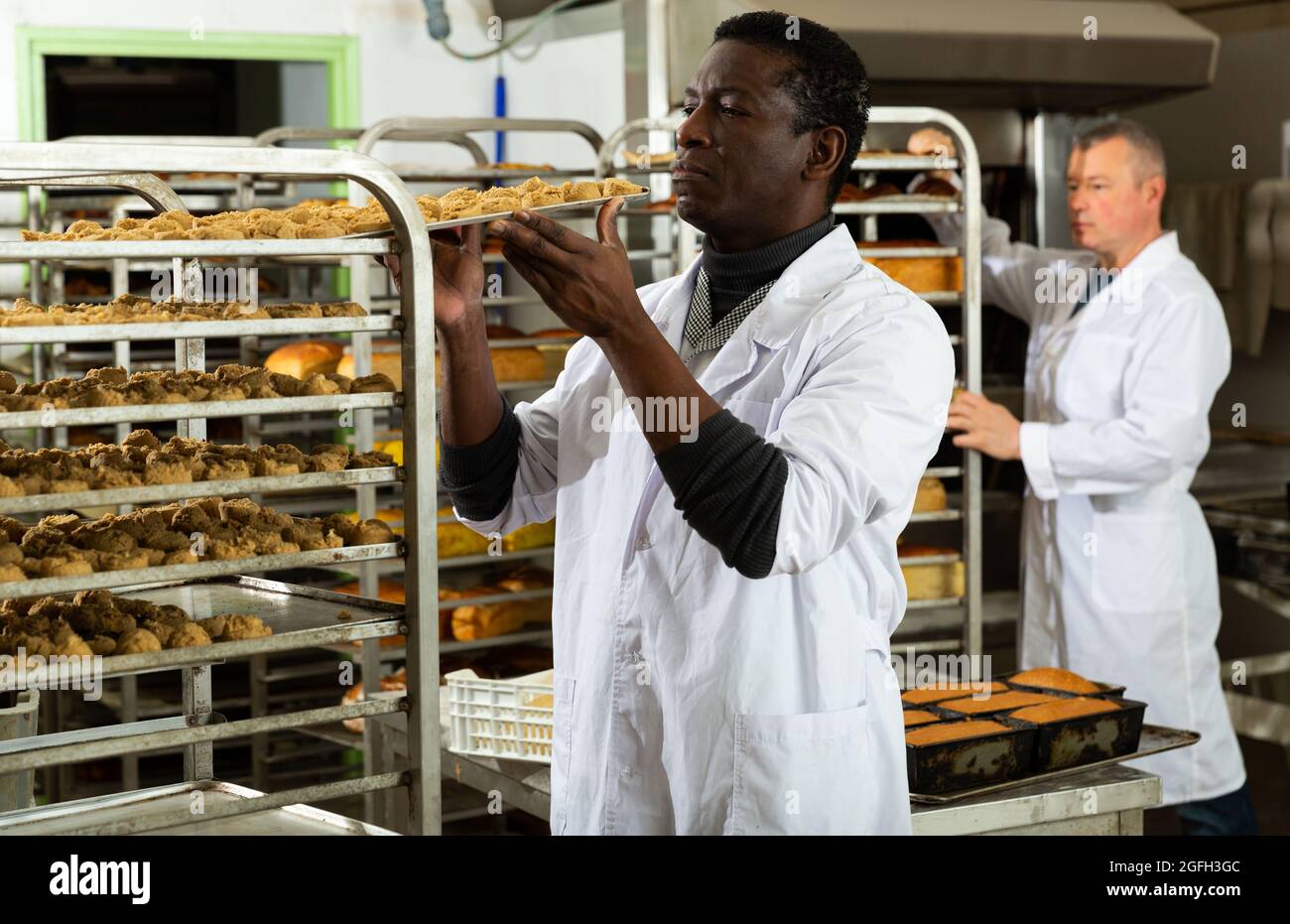 African baker arranging trays with bakery products on trolley Stock ...