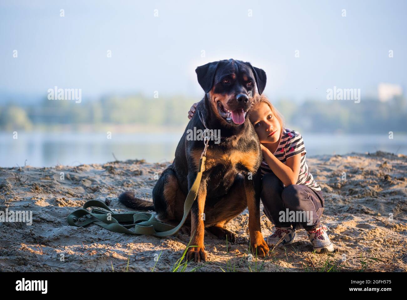 Little girl and rottweiler dog cuddling on the edge of a cliff enjoying ...