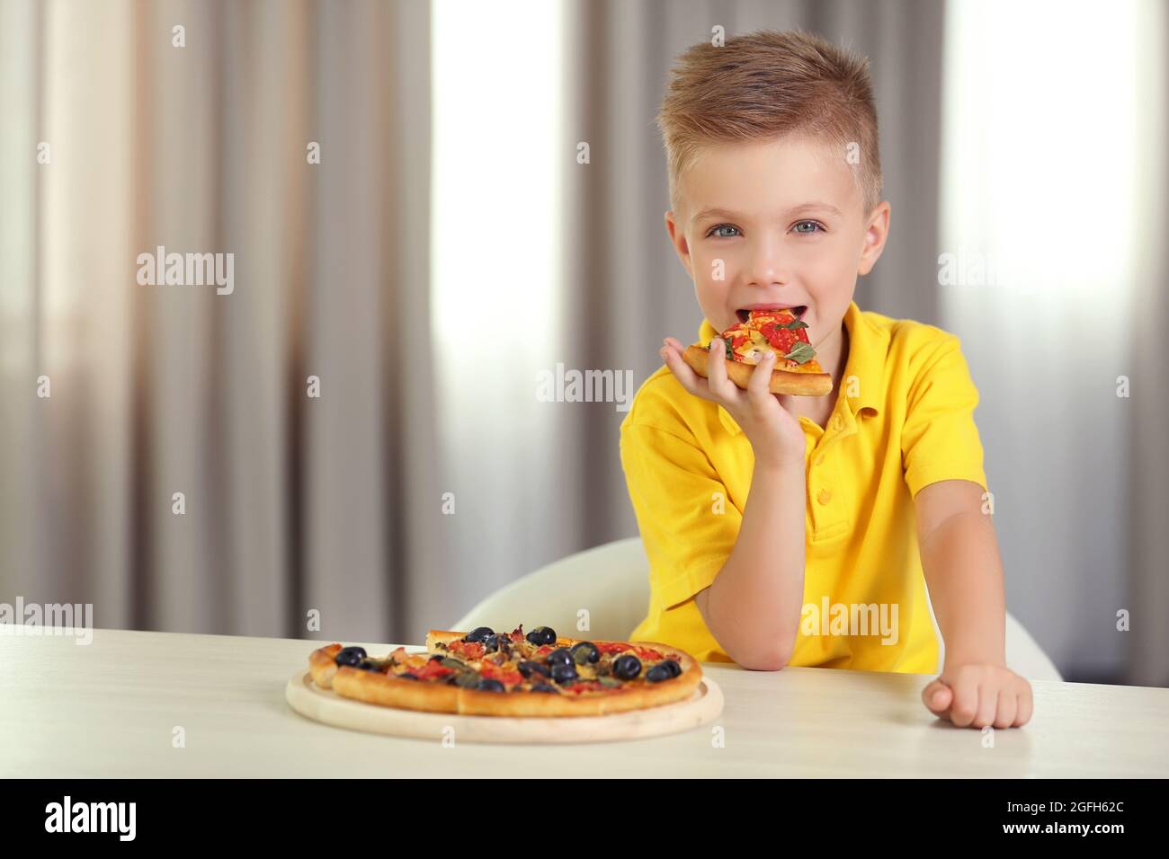 Cute boy eating pizza at home Stock Photo - Alamy
