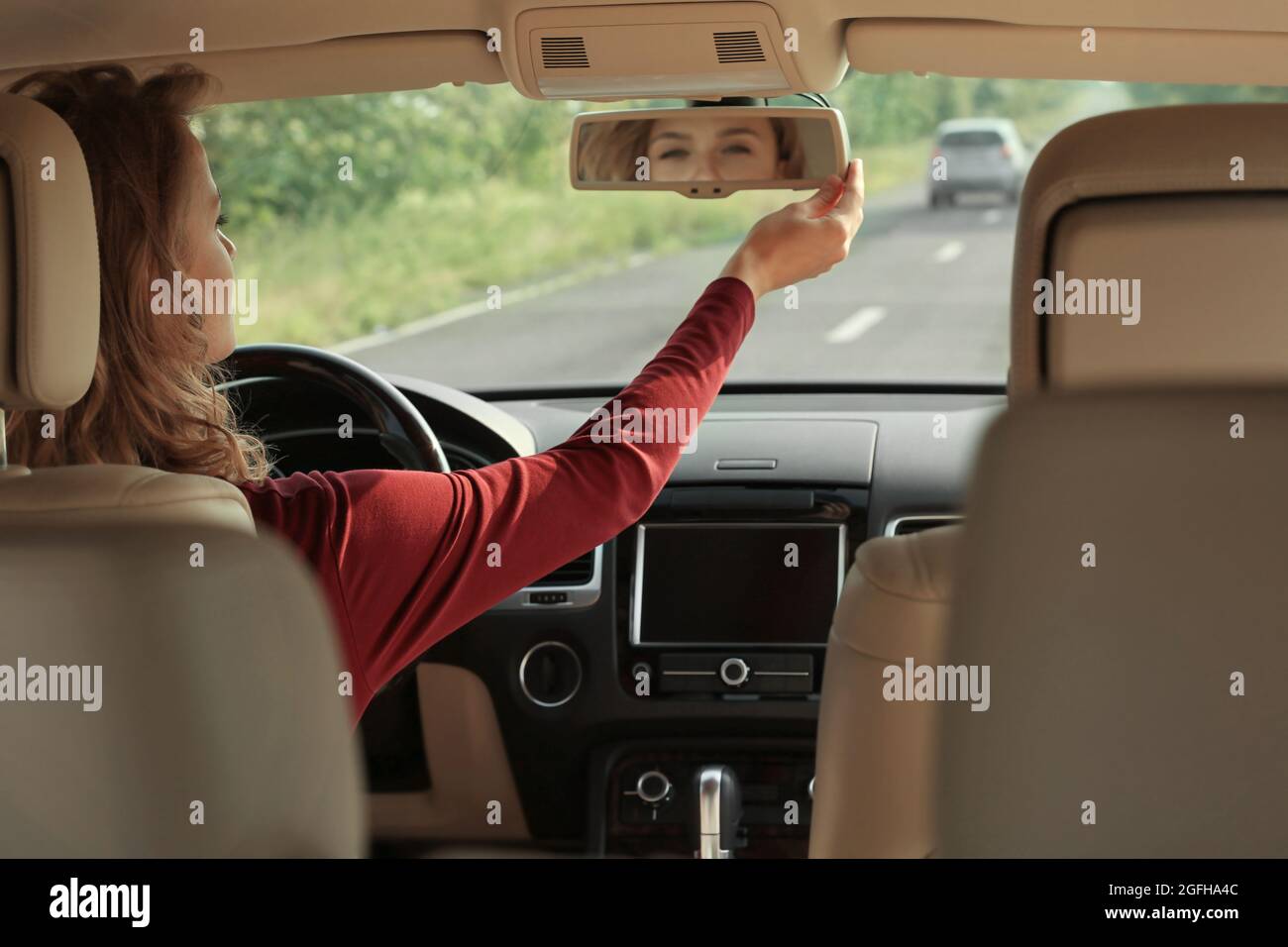 Pretty young woman looking in mirror while driving car Stock Photo - Alamy