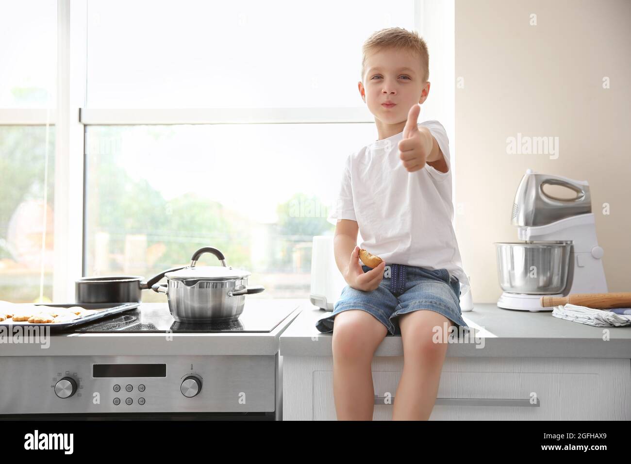 Cute little boy sitting on table in kitchen Stock Photo - Alamy