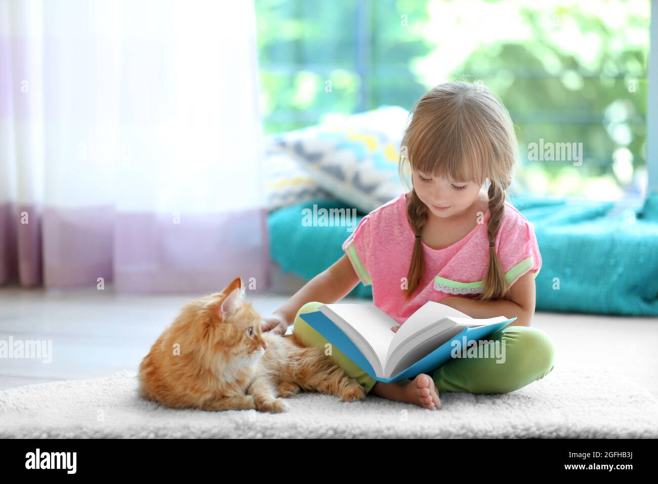 Red cat and cute little girl reading book on carpet Stock Photo - Alamy