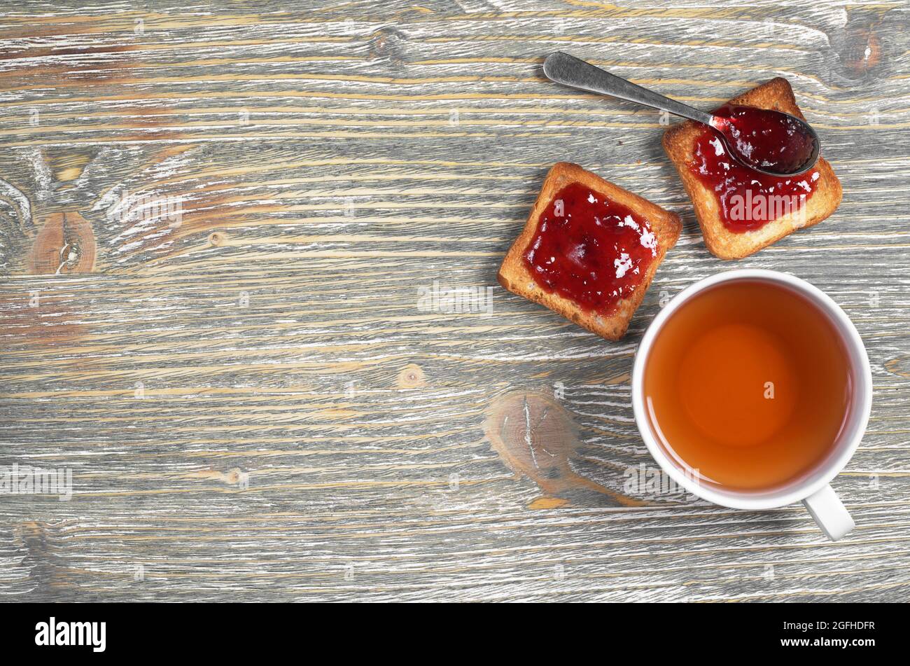 Cup of tea and small toast bread with jam on old wooden background, top ...
