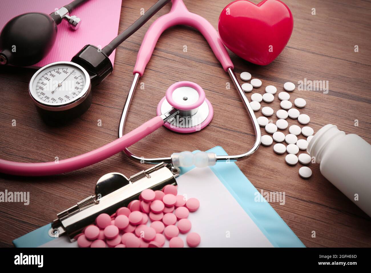 Pink stethoscope, pills and other medical equipment on wooden ...