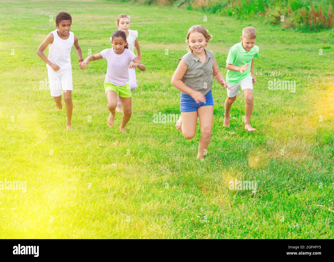 Multiracial group of cheerful tweens running together in city park ...
