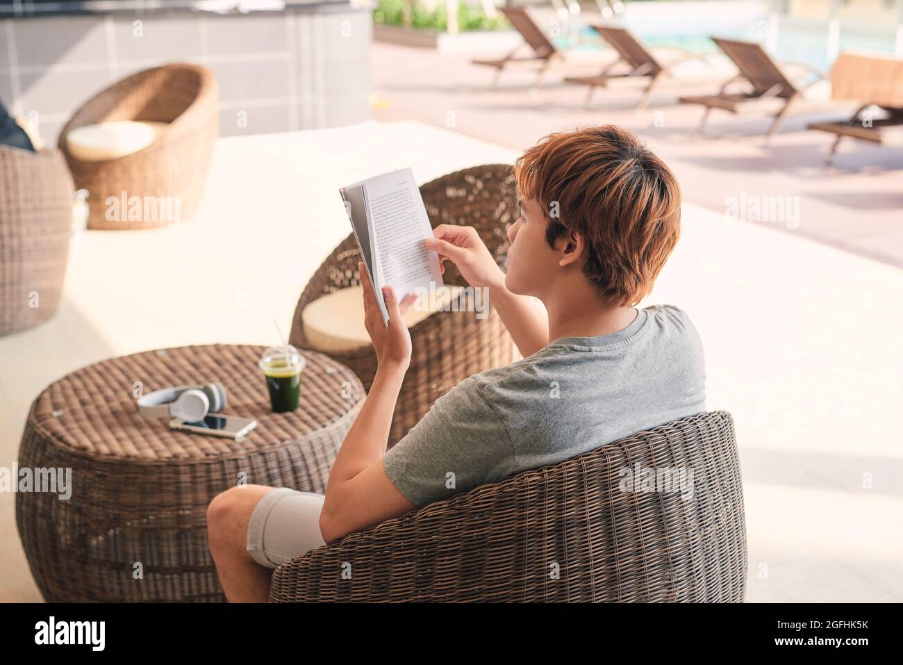 young man lying on the chaise-lounge and reading a book near the ...