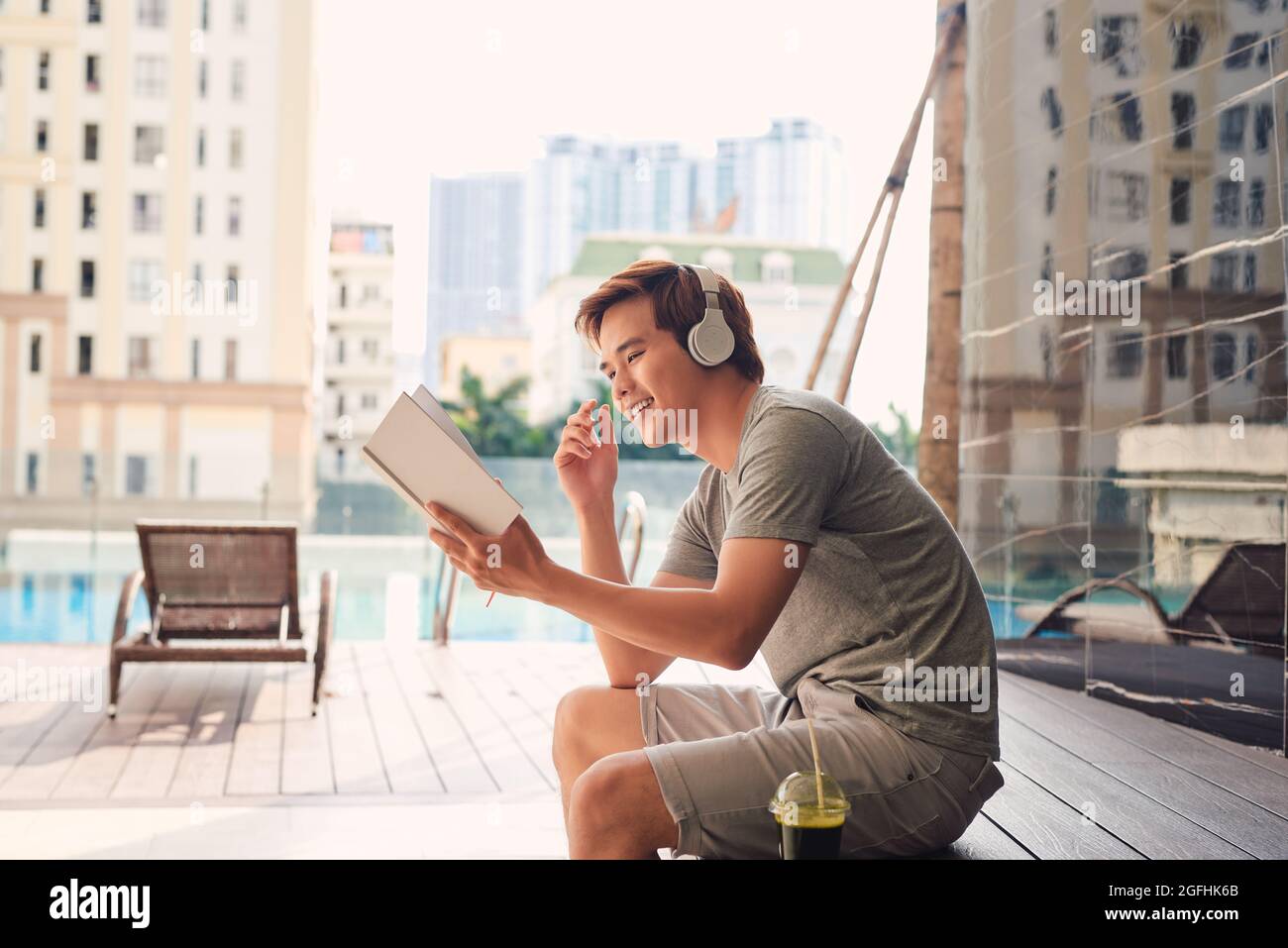 Young man with headphone near swimming pool reading book Stock Photo ...