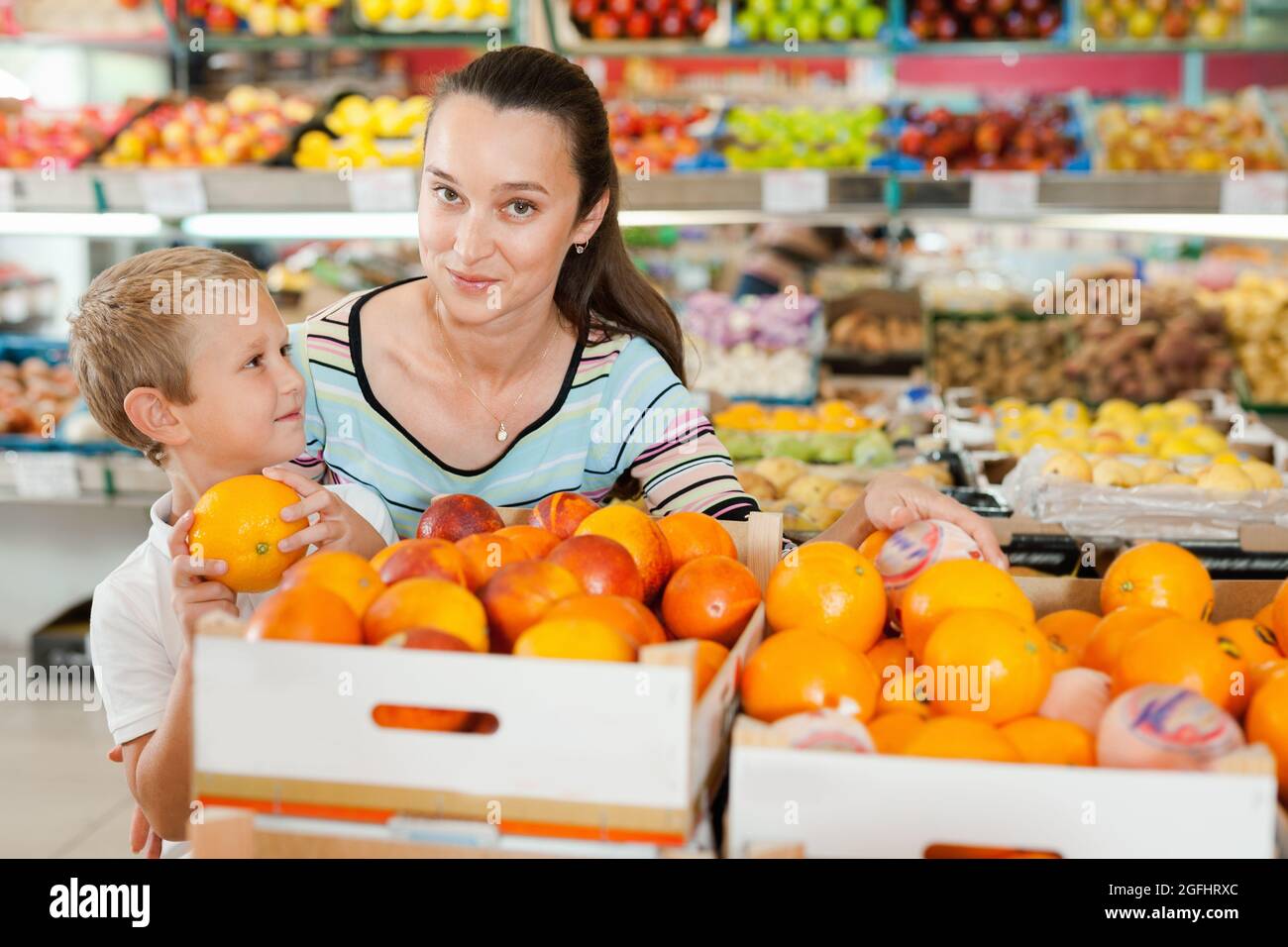 Portrait of happy woman and her little son choosing oranges at shop ...