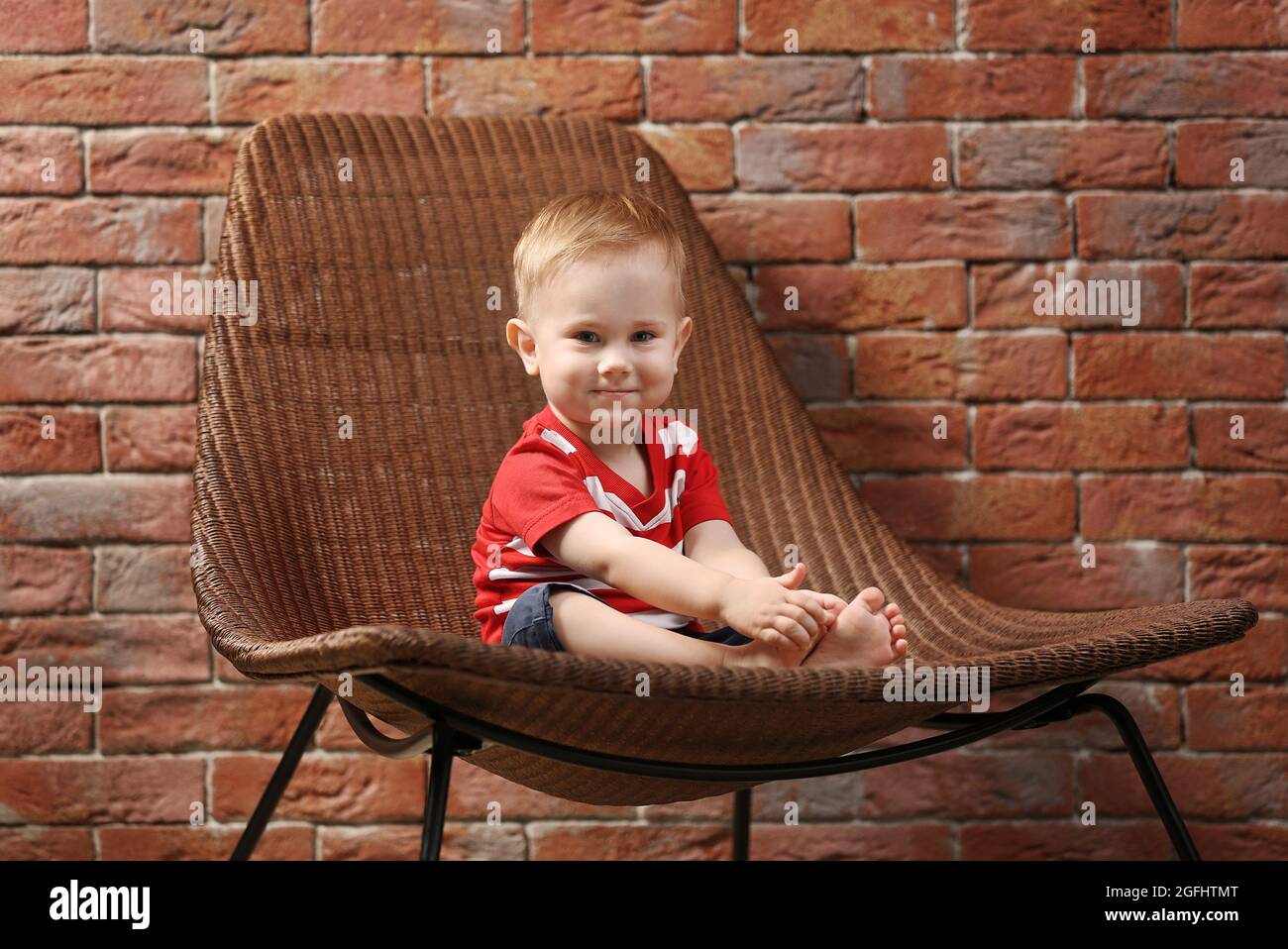 Cute baby boy sitting in a designer chair on a brick wall background ...