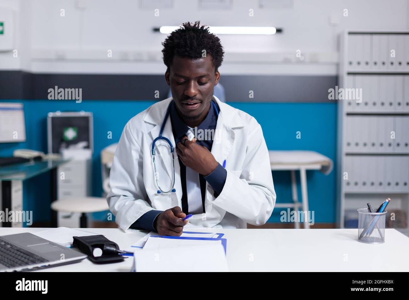 Portrait of african american doctor sitting at desk in medical cabinet ...