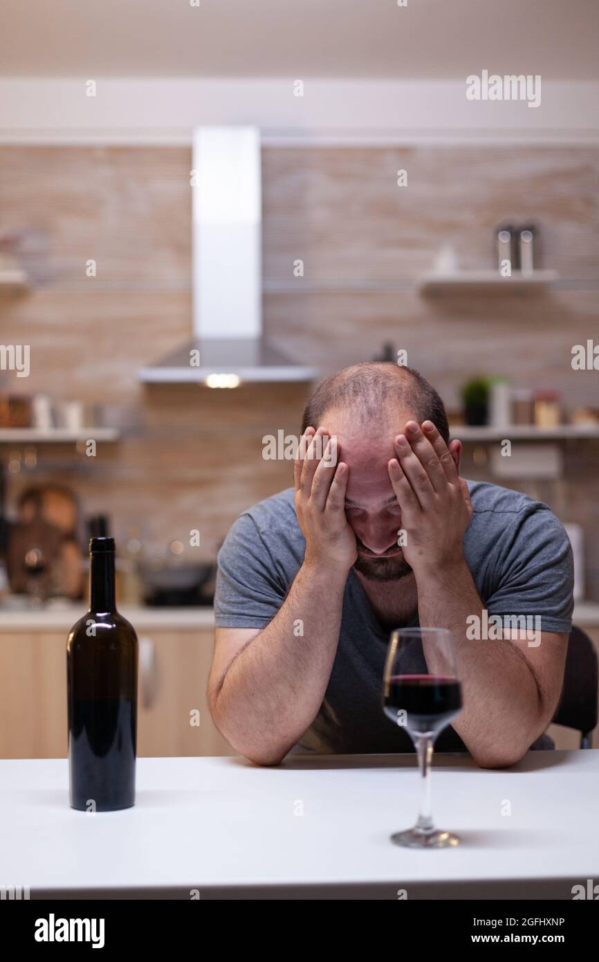 Desperate man feeling miserable while having glass with wine and bottle ...