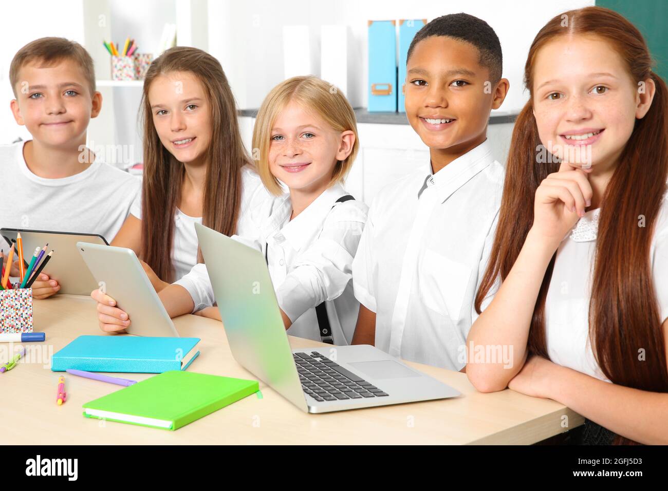 Schoolchildren sitting in classroom with laptop and tablet computers ...
