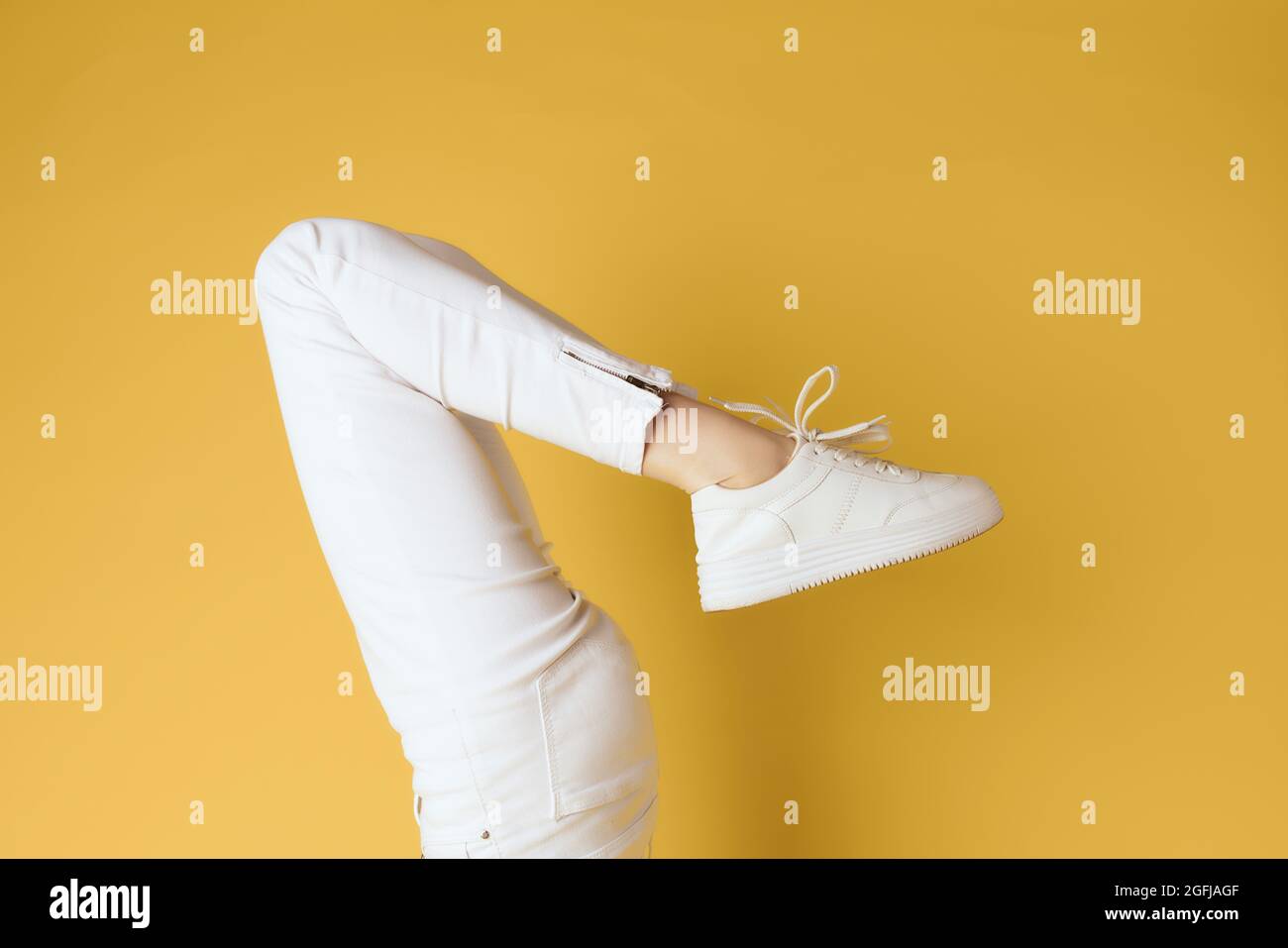 female inverted legs in white sneakers cropped view yellow background ...