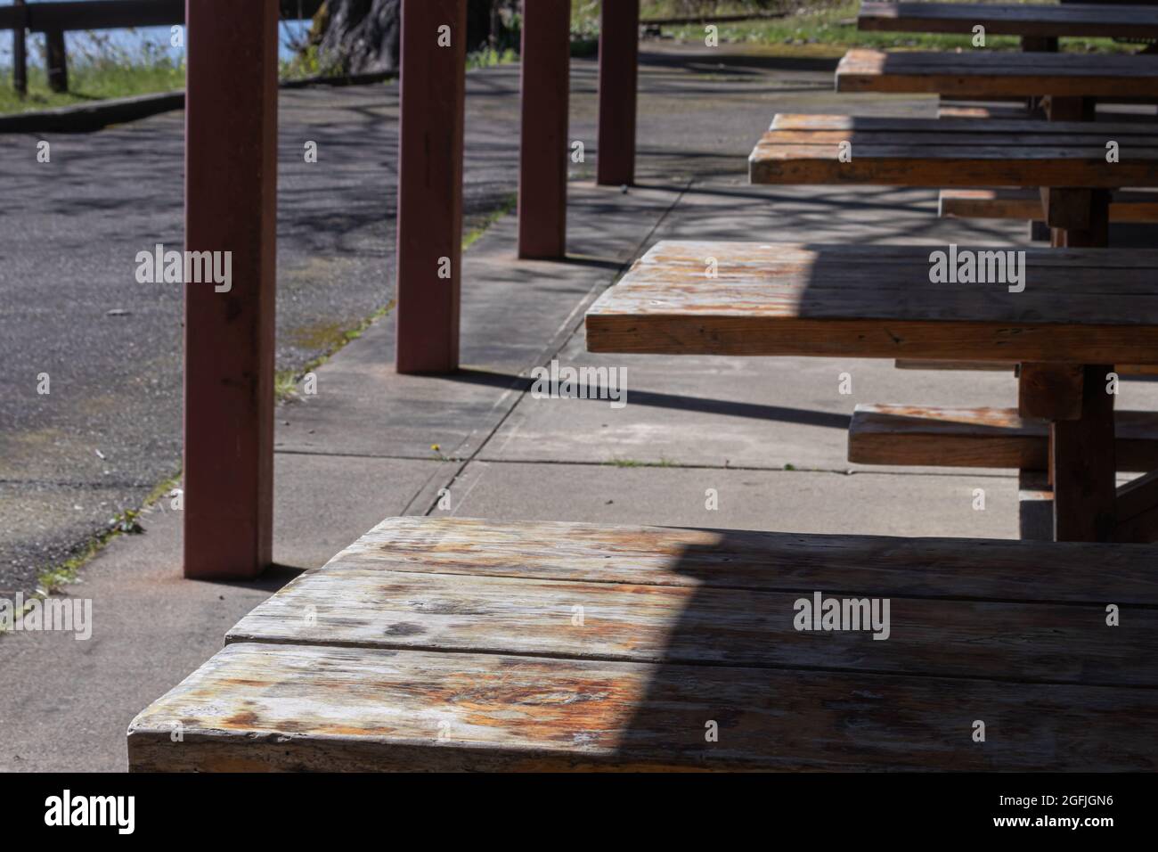 empty wooden picknick tables lined up in a row underneath a pavilion ...