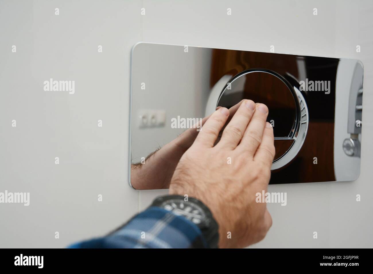 A man is pressing a wall-mounted polished chrome single flush plate to ...