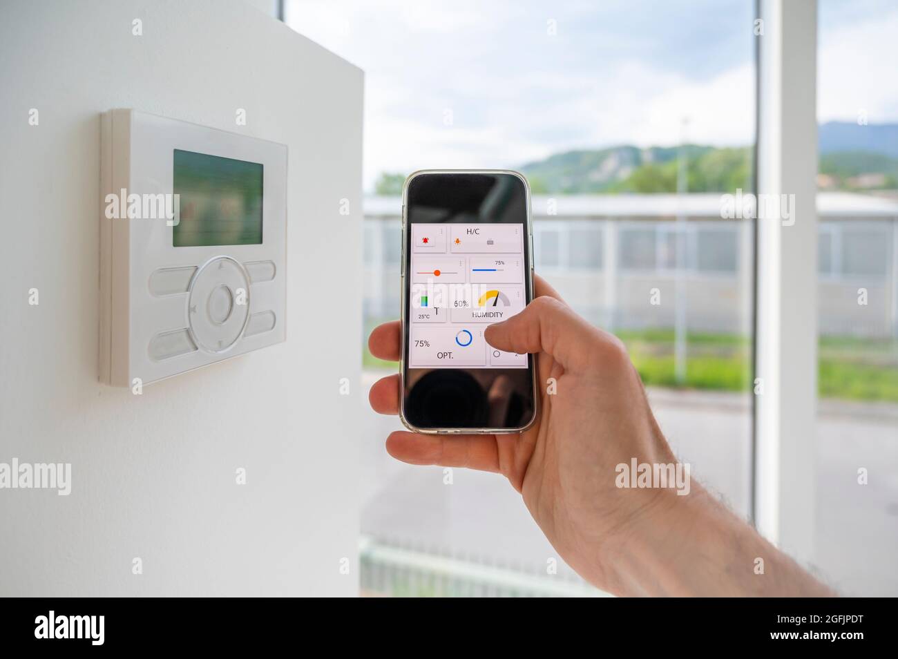 Hand holding a mobile phone showing an home automation app to manage ...