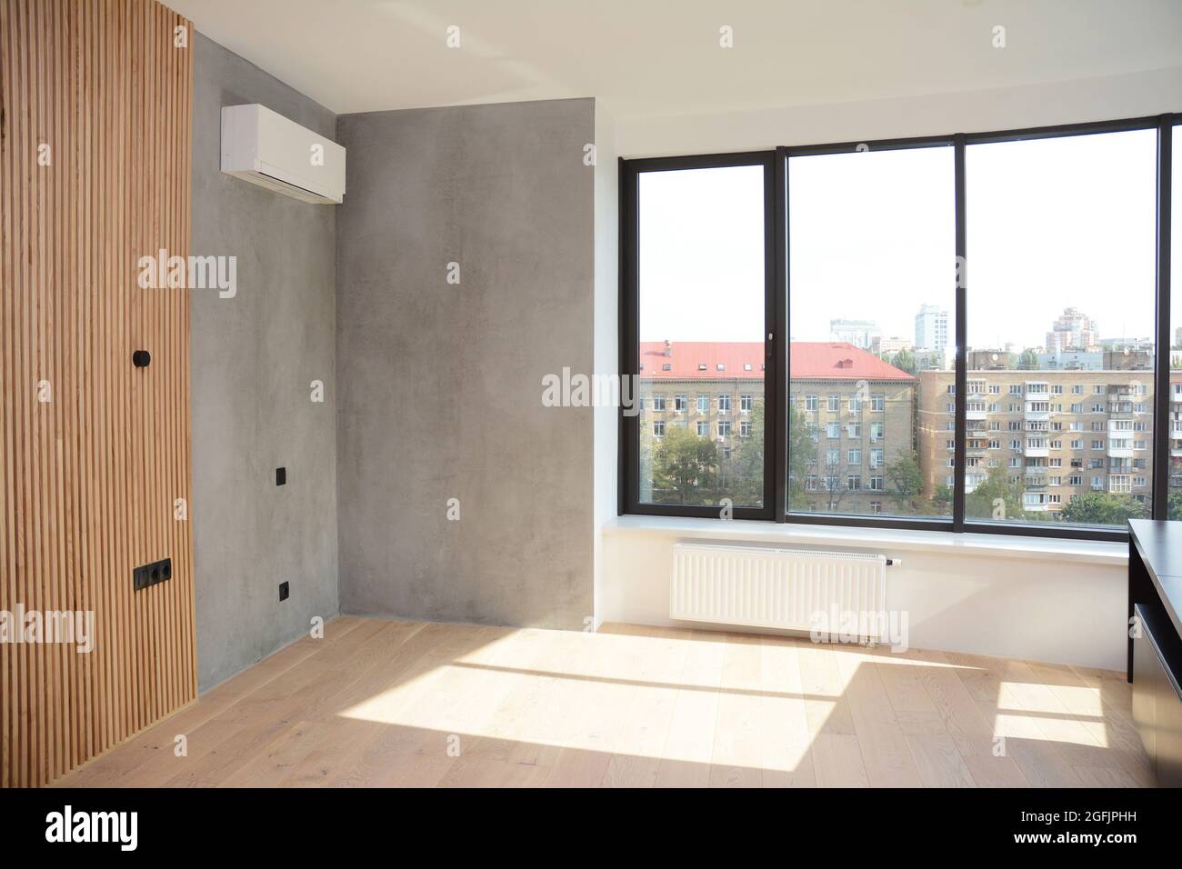 An empty apartment room with a large window and radiator heater, wood ...