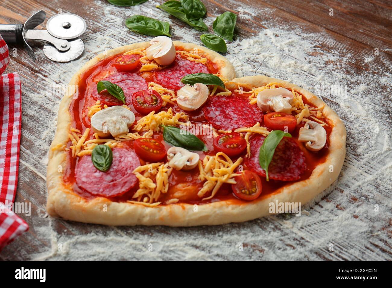 Unbaked pizza in heart shape with ingredients on table Stock Photo - Alamy
