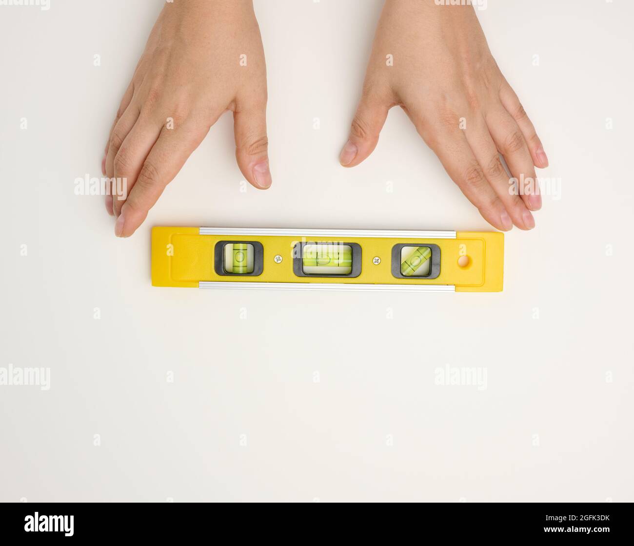 female hands holds a yellow plastic building level on a white ...