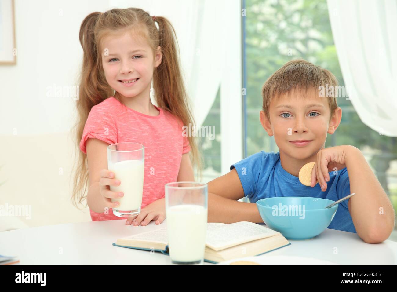 Little boy and girl sitting at table with glasses of milk and book ...