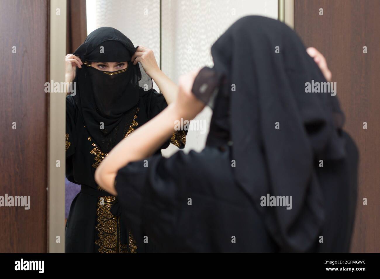 A Muslim woman dresses up in front of a mirror and puts on a burqa in ...