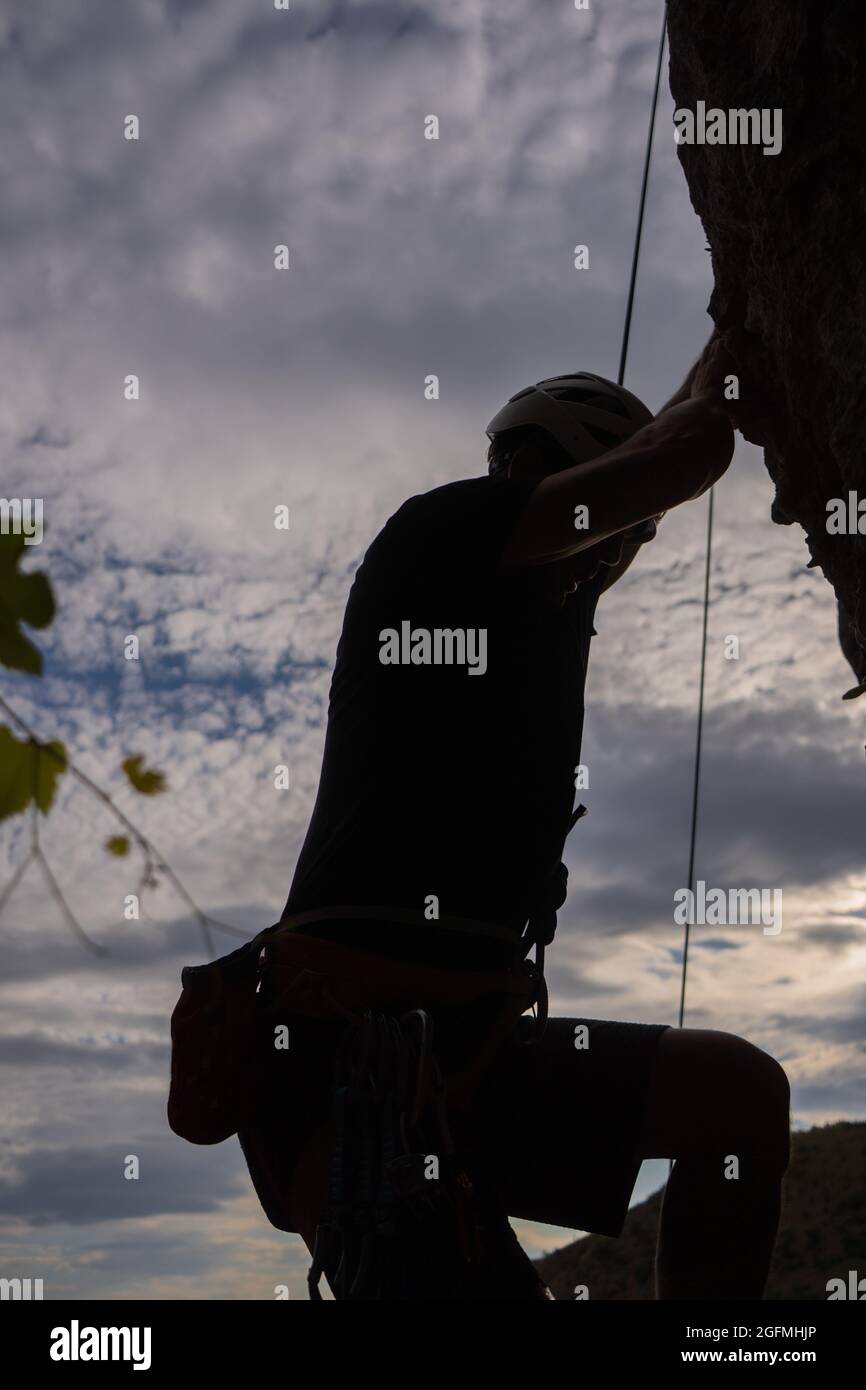 Silhouette of senior guy climbing the high hill with his equipment ...