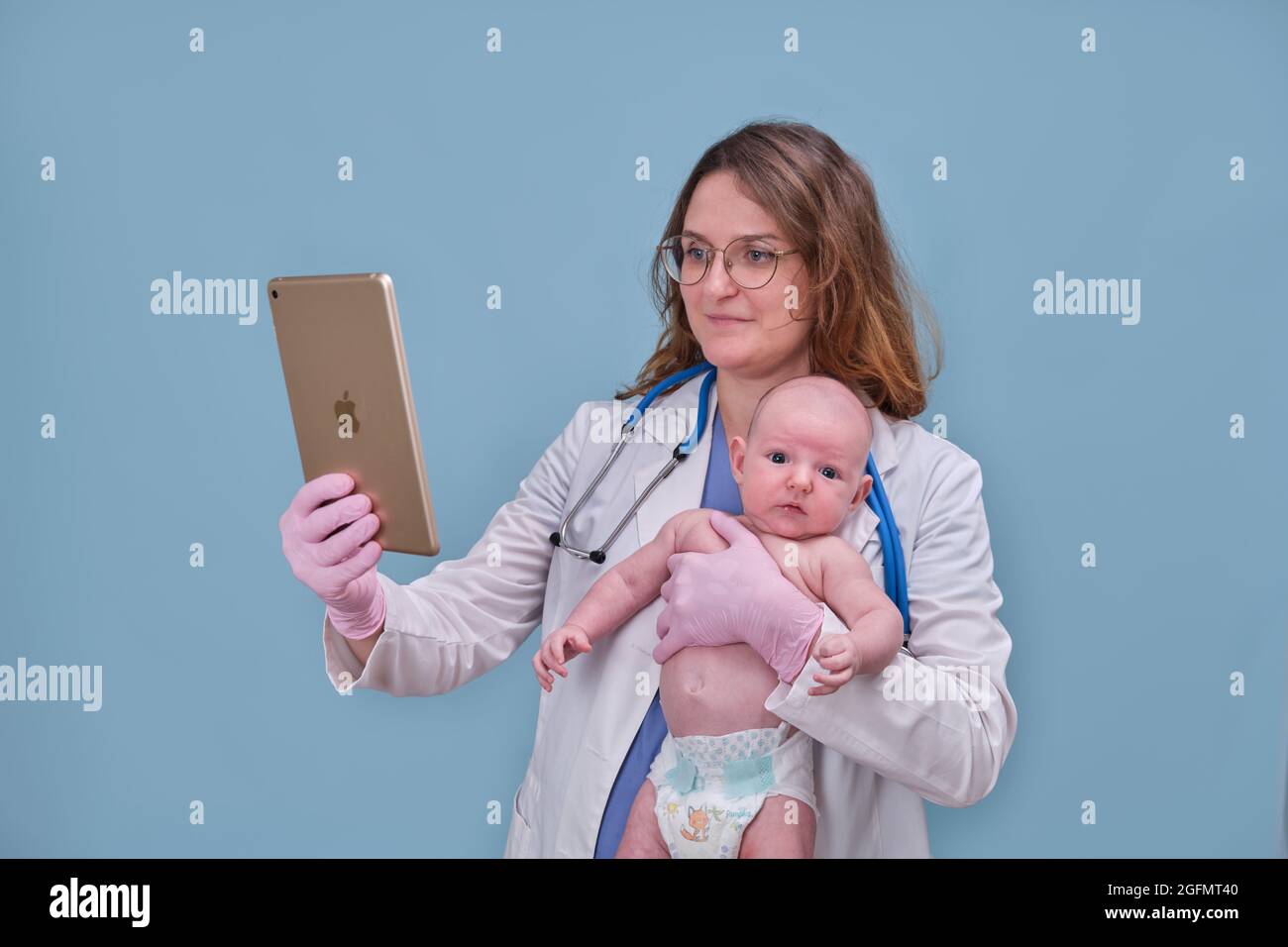 Pediatrician doctor holding apple ipad and newborn baby, blue studio ...