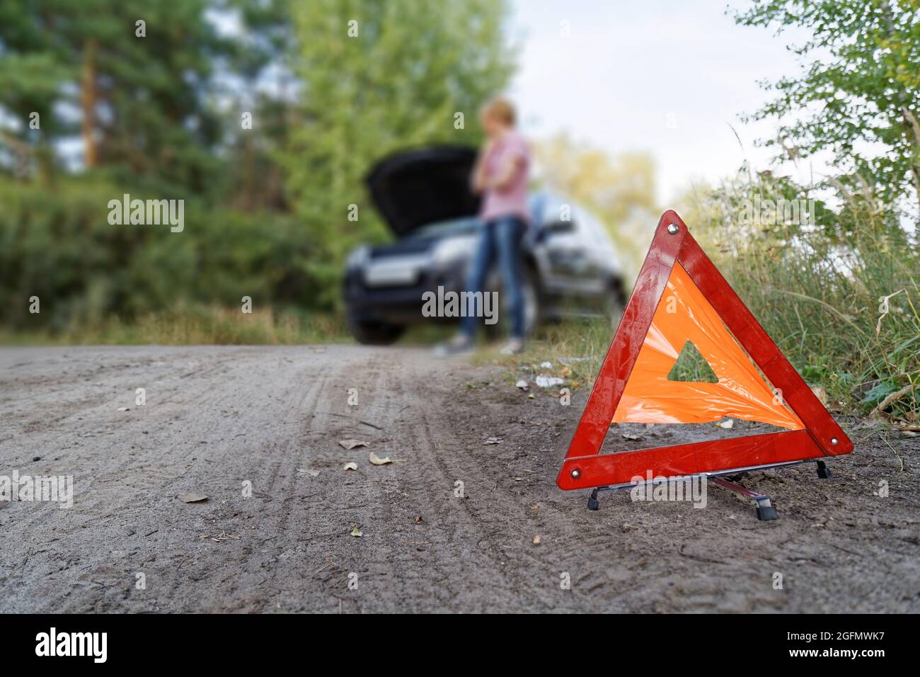 Emergency Warning Triangle on rural roadside. Girl near broken car with ...