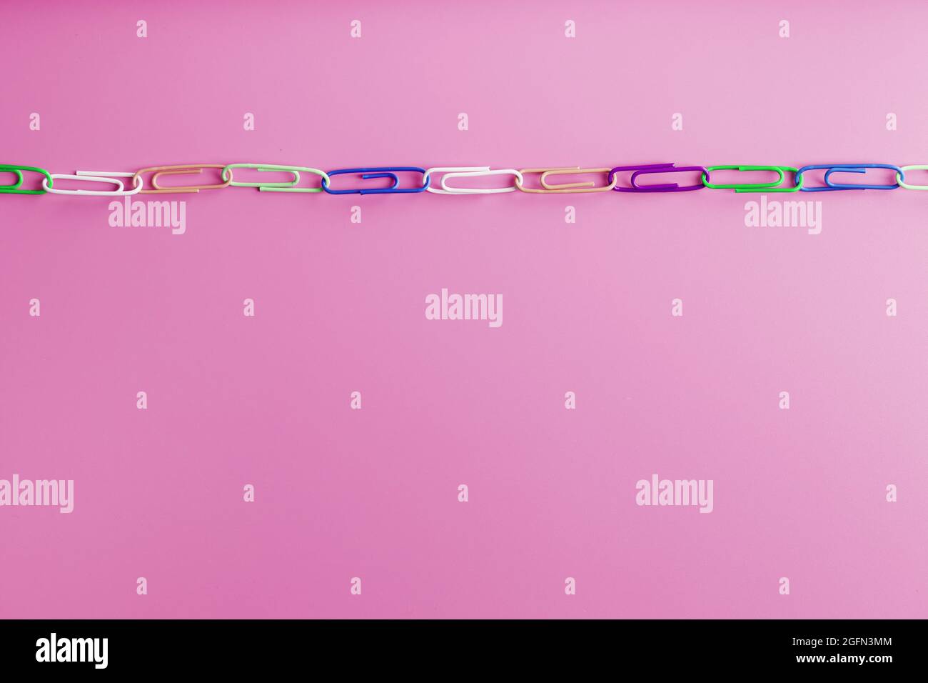 Multicolored paper clips are attached in a row on a pink background ...