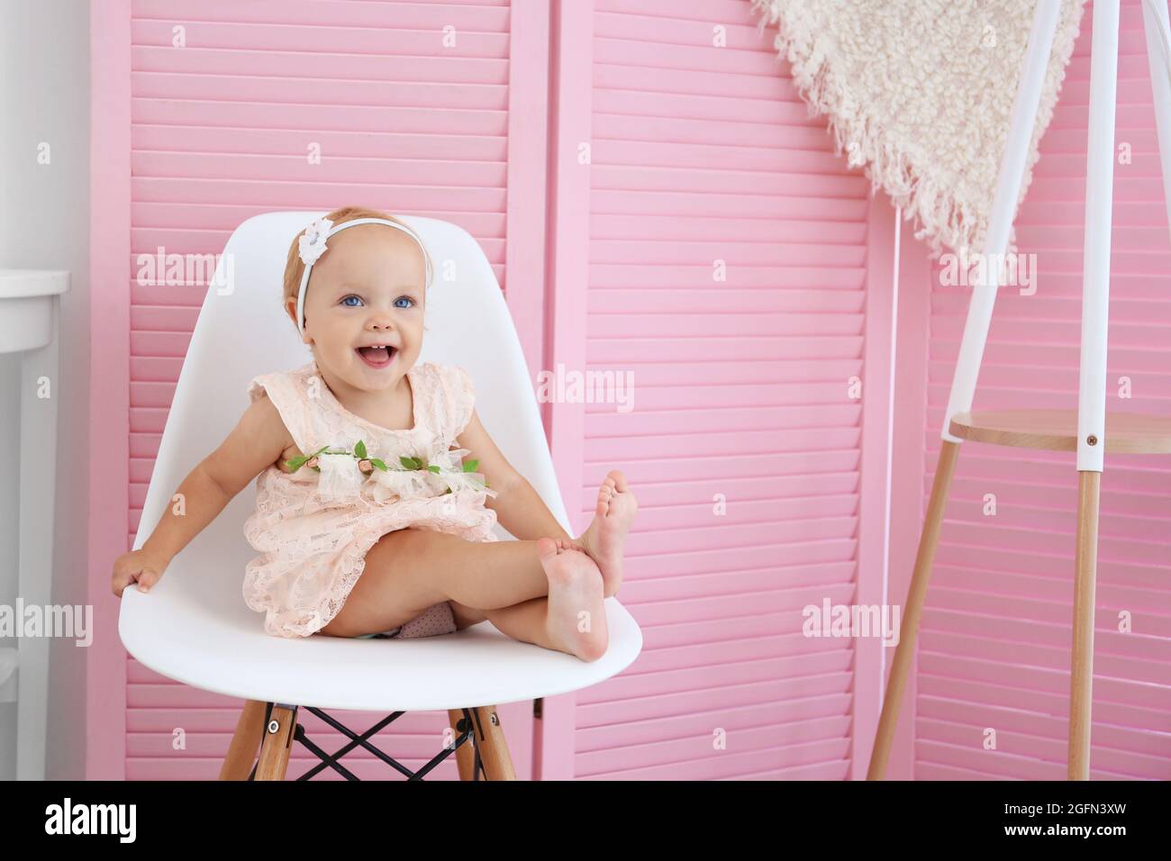 Little baby girl sitting on chair on pink wooden screen background ...