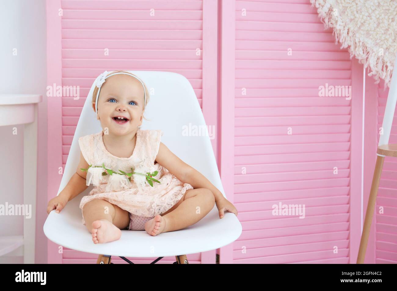 Little baby girl sitting on chair on pink wooden screen background ...