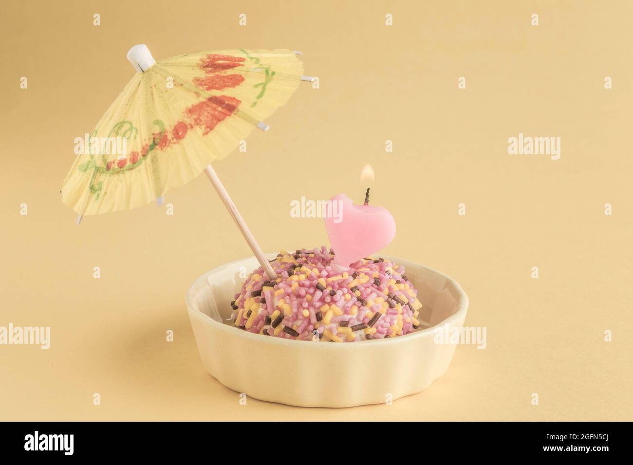 A small birthday cake with heart shaped candle and umbrella on yellow ...