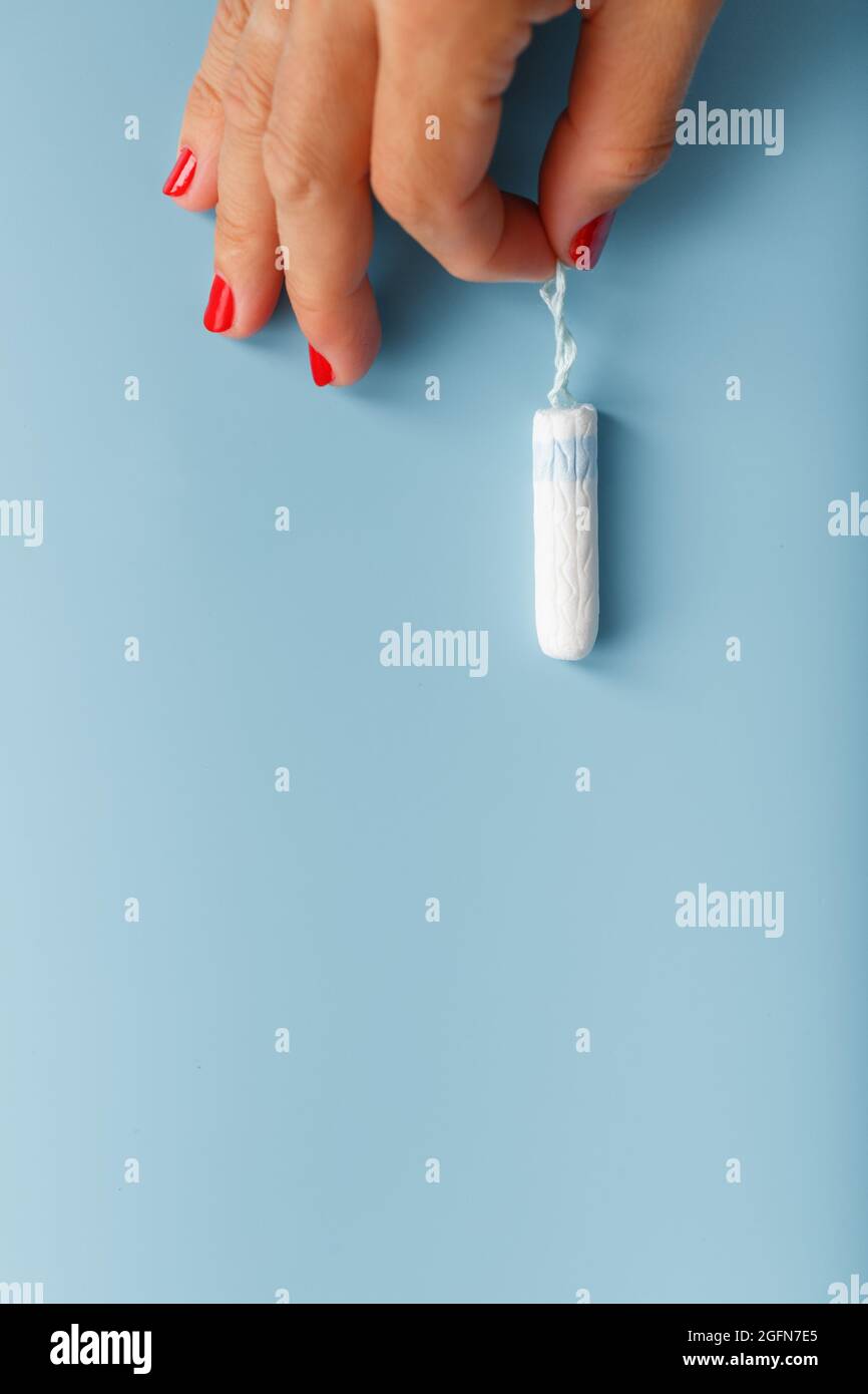 Female fingers with red nails hold a female sanitary swab on a blue ...