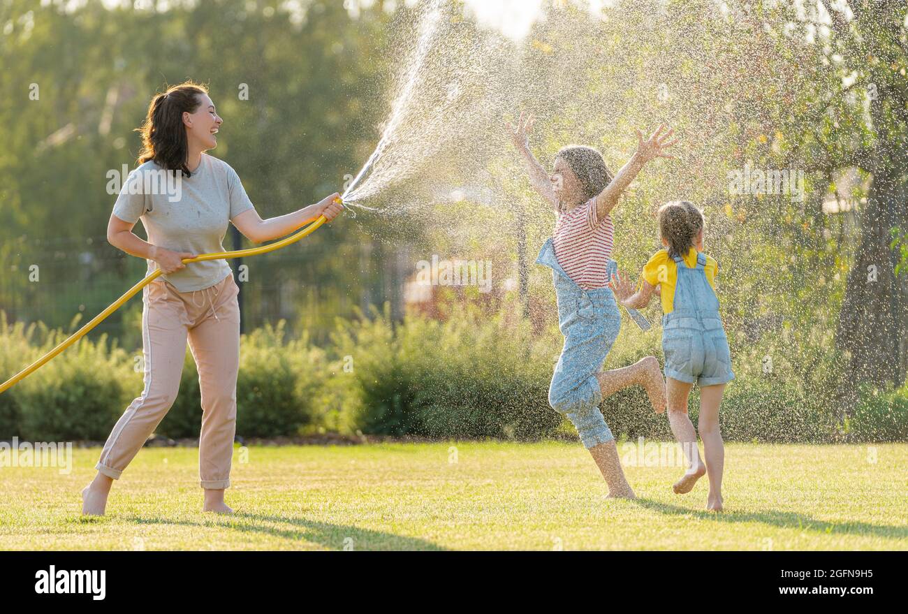 Happy family playing in backyard. Mother sprinkling her kids in hot ...