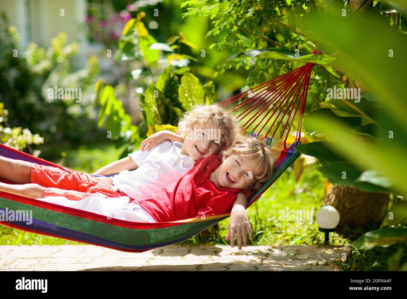Kids relax in colorful rainbow hammock. Hot day garden outdoor fun. Boy ...